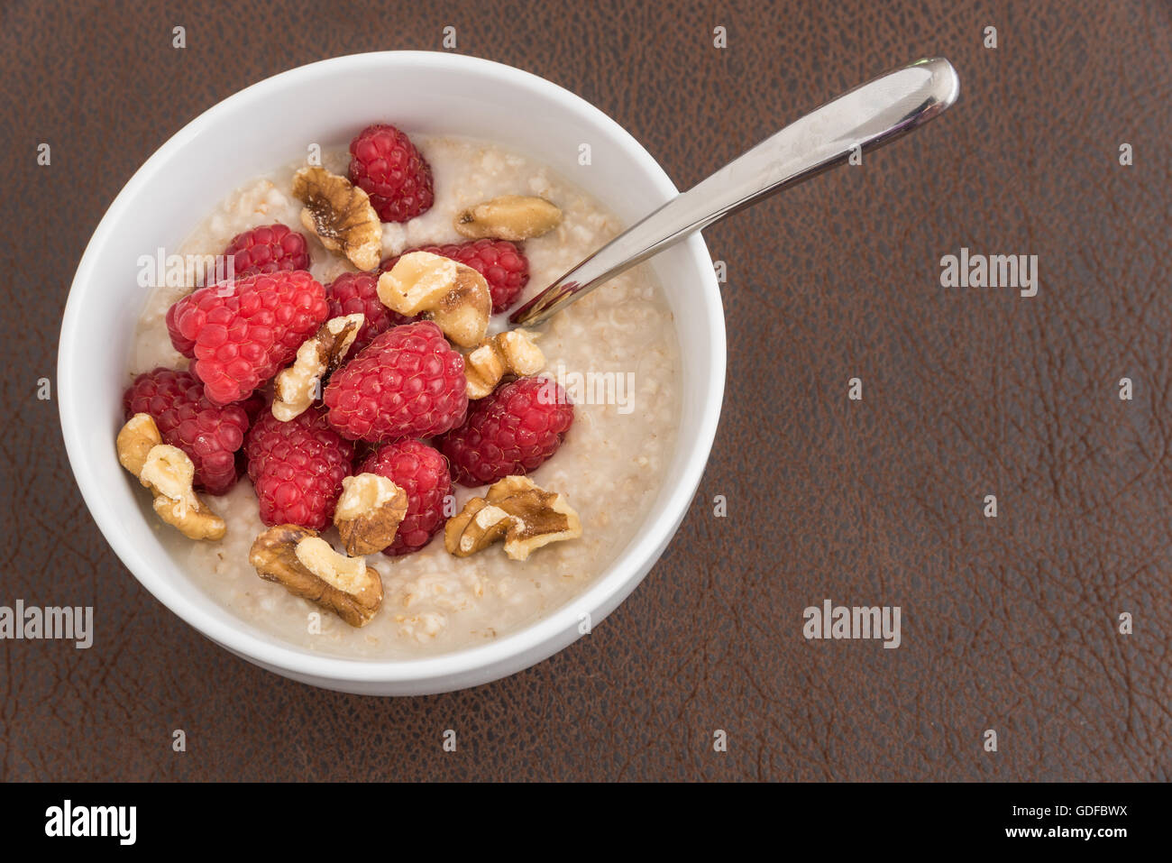 Spoon dipping into fresh picked raspberries and walnuts topping oatmeal ...