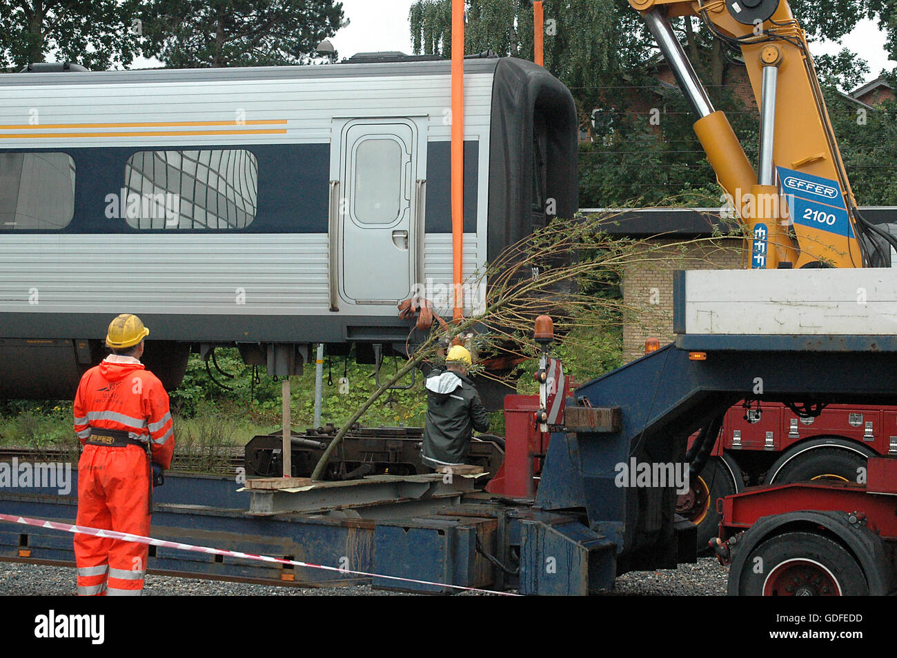 Railway carriage lifted by crane. A helper holds a small tree aside to ...