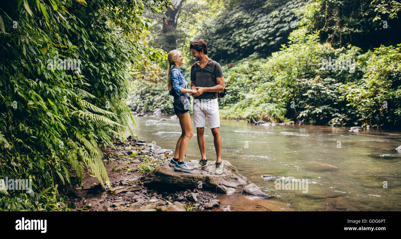 Loving young couple standing together by a mountain stream in forest ...