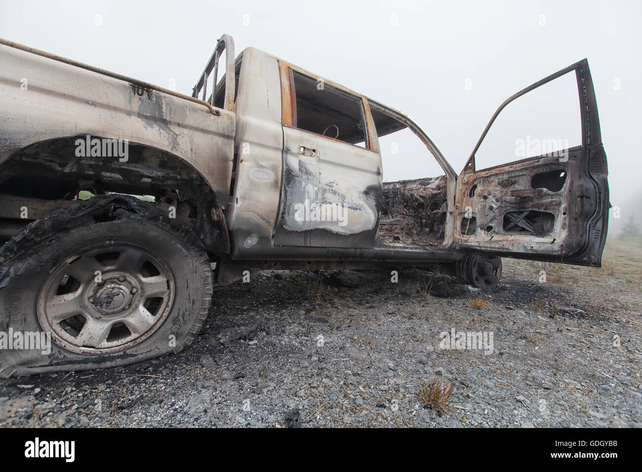 Low and wide shot of a burnt out pick up truck left abandoned on public ...