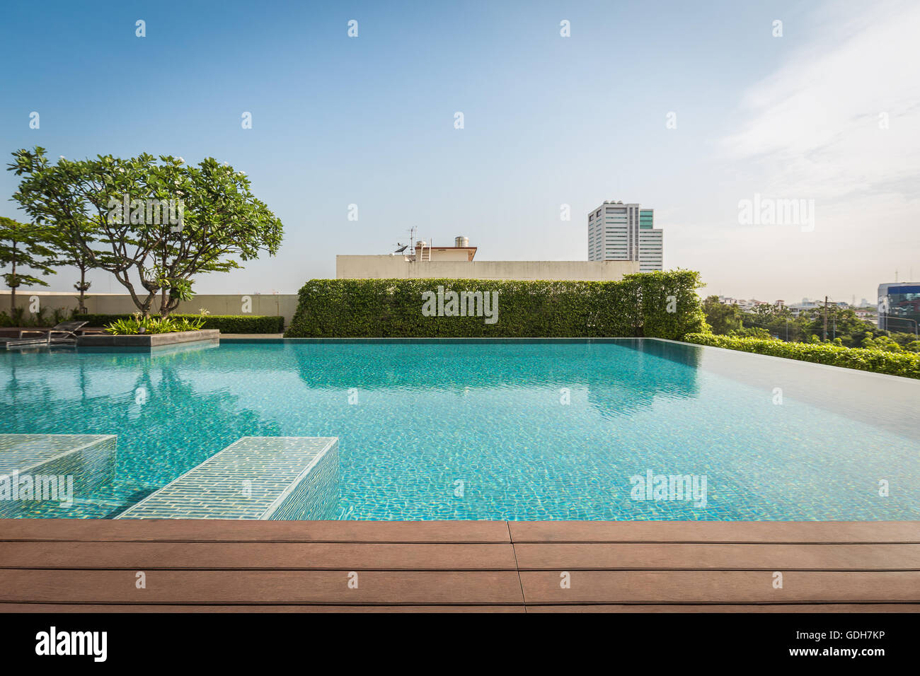 Wooden floor close to reflecting mosaic swimming pool which surround by ...