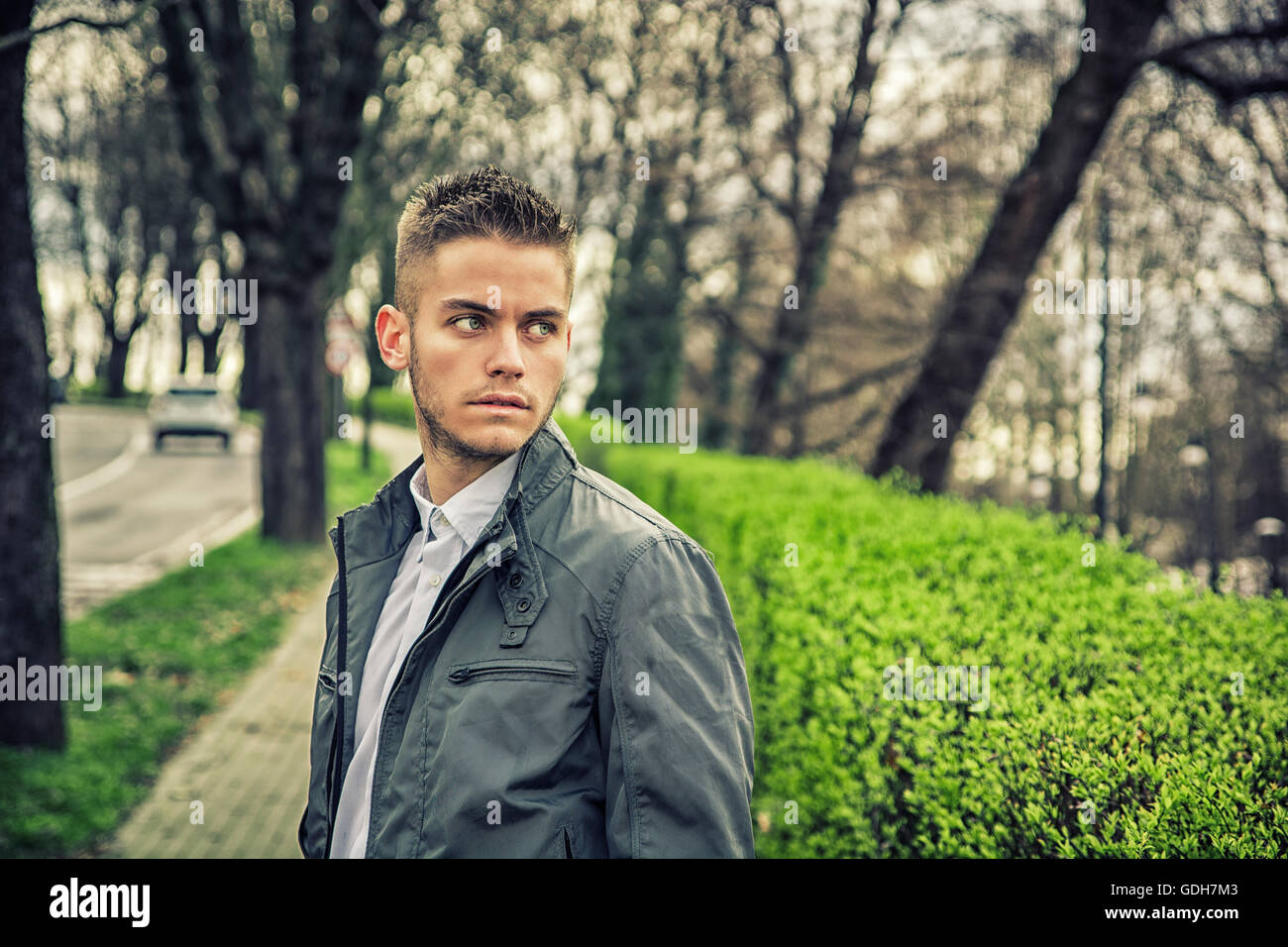Portrait of handsome young man looking to a side while sitting in city ...