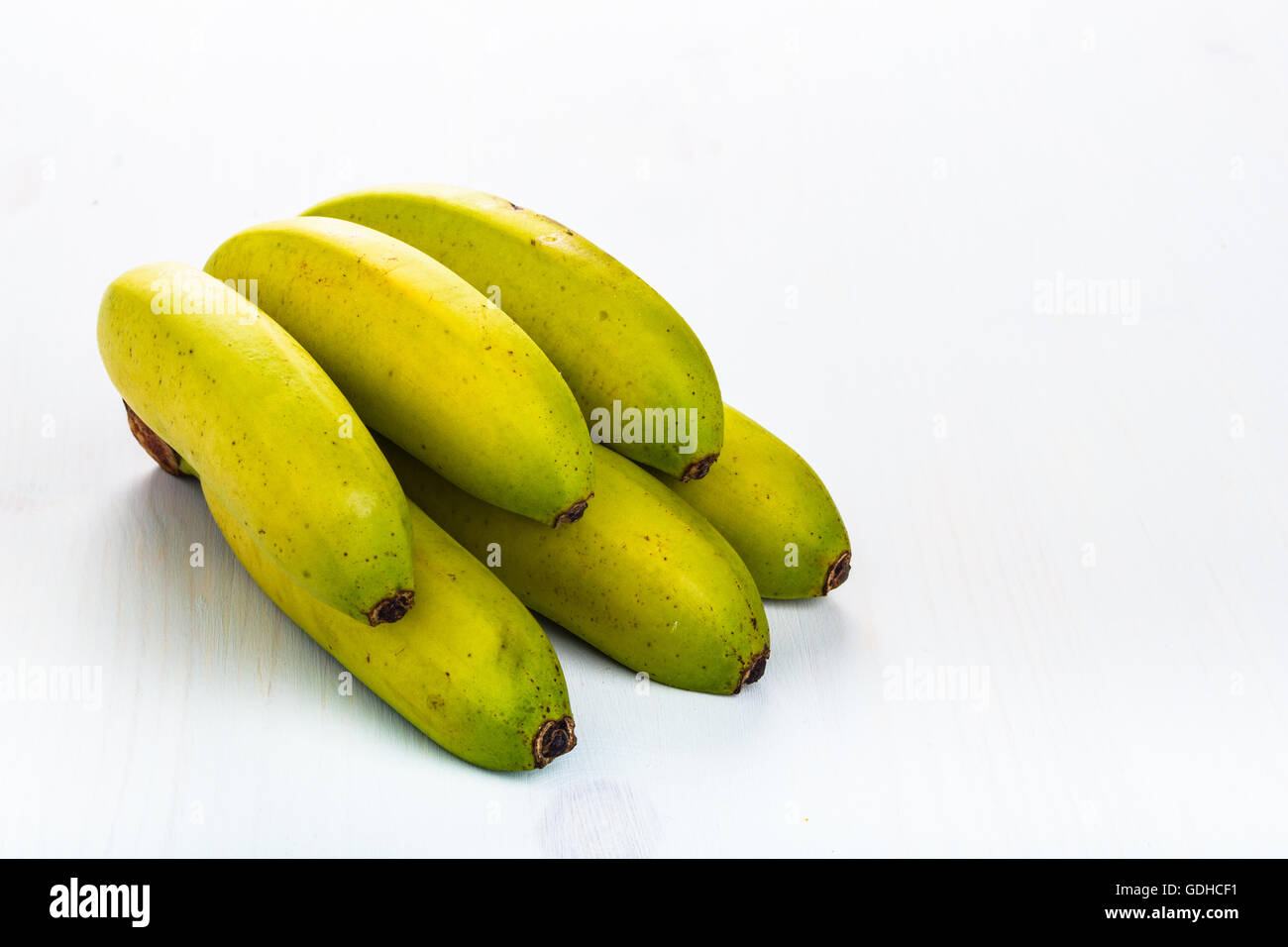 Small green bananas isolated on white timber board Stock Photo - Alamy