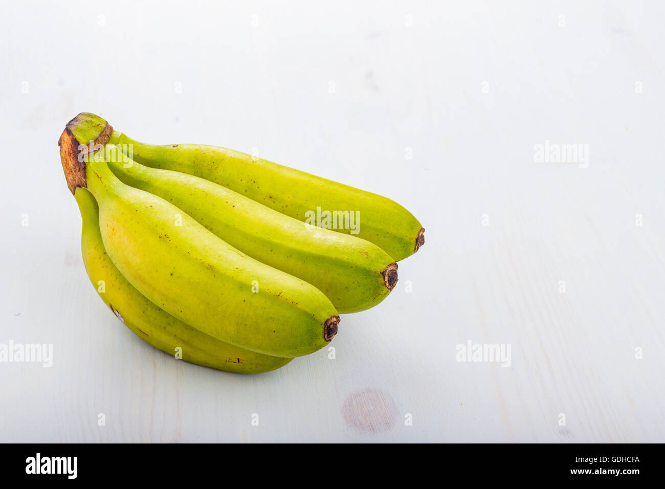Small green bananas isolated on white timber board Stock Photo - Alamy