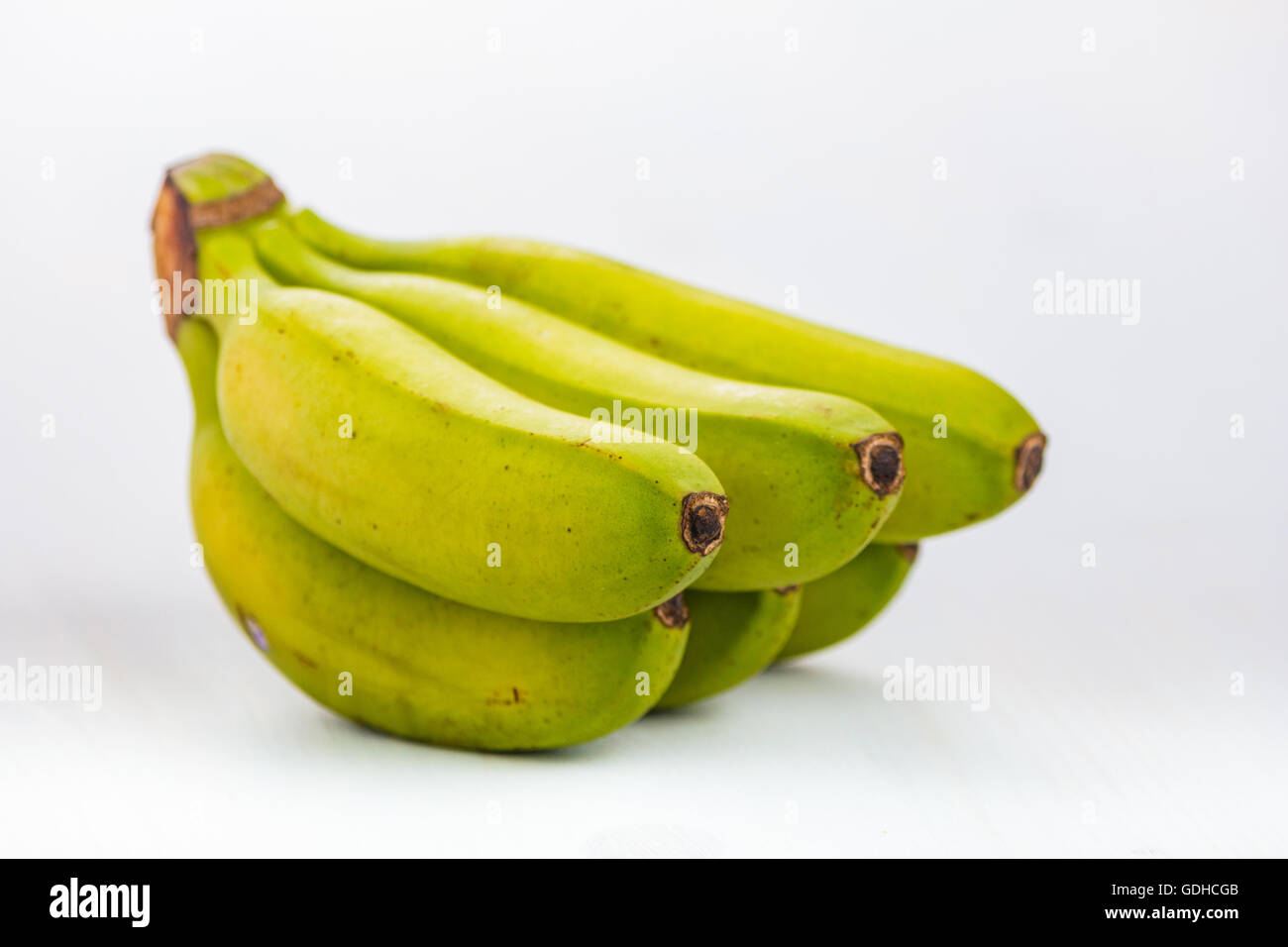 Small green bananas isolated on white timber board Stock Photo - Alamy