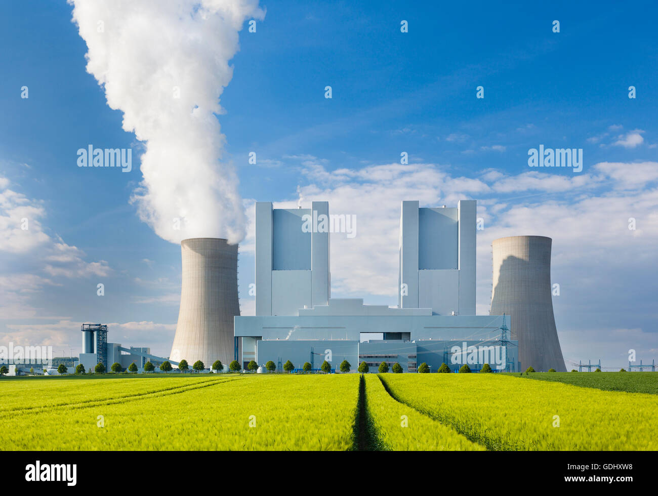 A shiny new lignite power station behind a rye field with wheel tracks ...