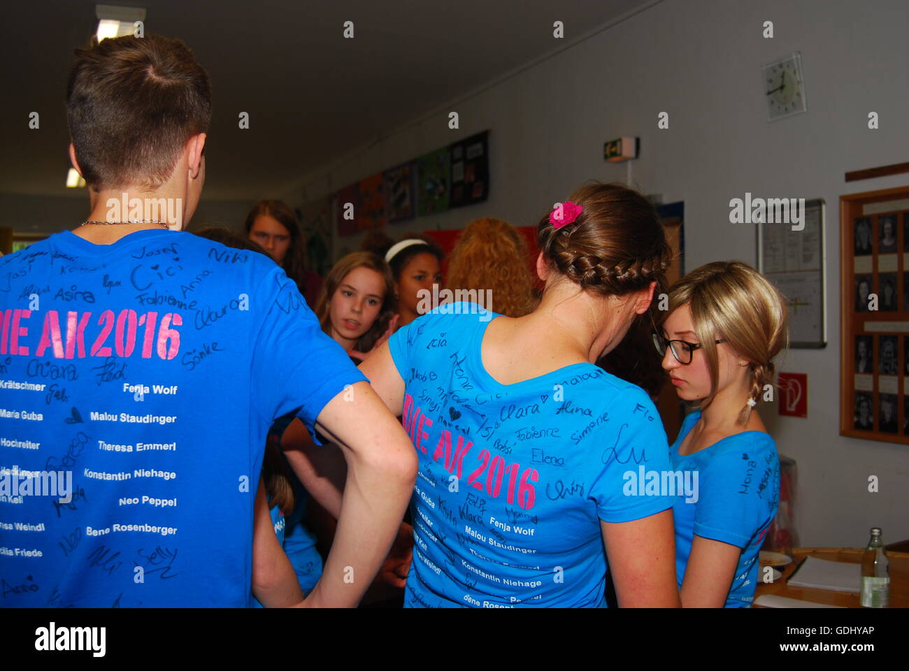 A group of high school students sign each other's t-shirts as they say ...