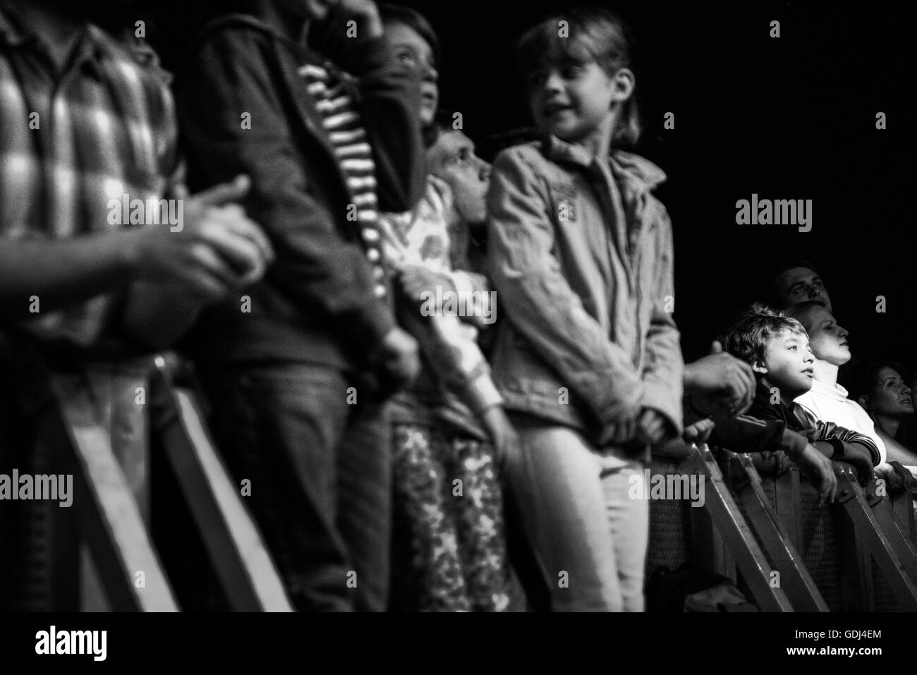 Small boy on the fence of the first row at the concert at night ...