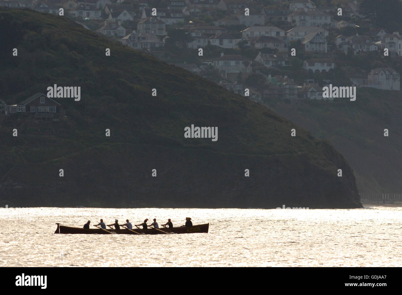 Gig rowing past the headland at sunset Stock Photo - Alamy