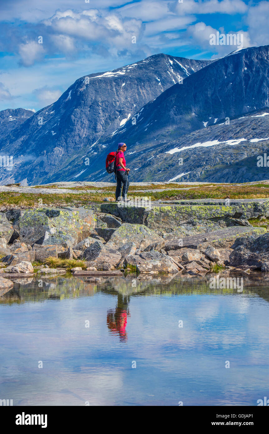 Solitary female walker hiker in red with reflection in wild mountains ...
