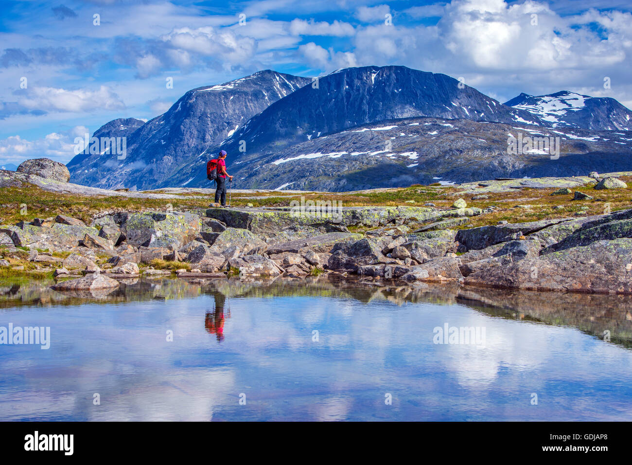 Solitary female walker hiker in red with reflection in wild mountains ...