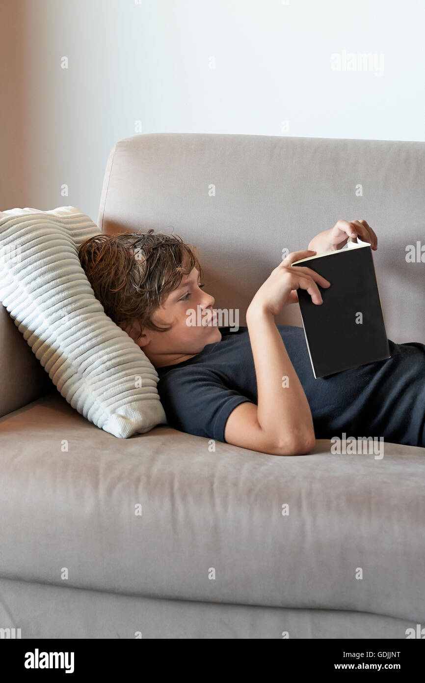 Young boy reading a book on sofa after his shower, indoor Stock Photo ...
