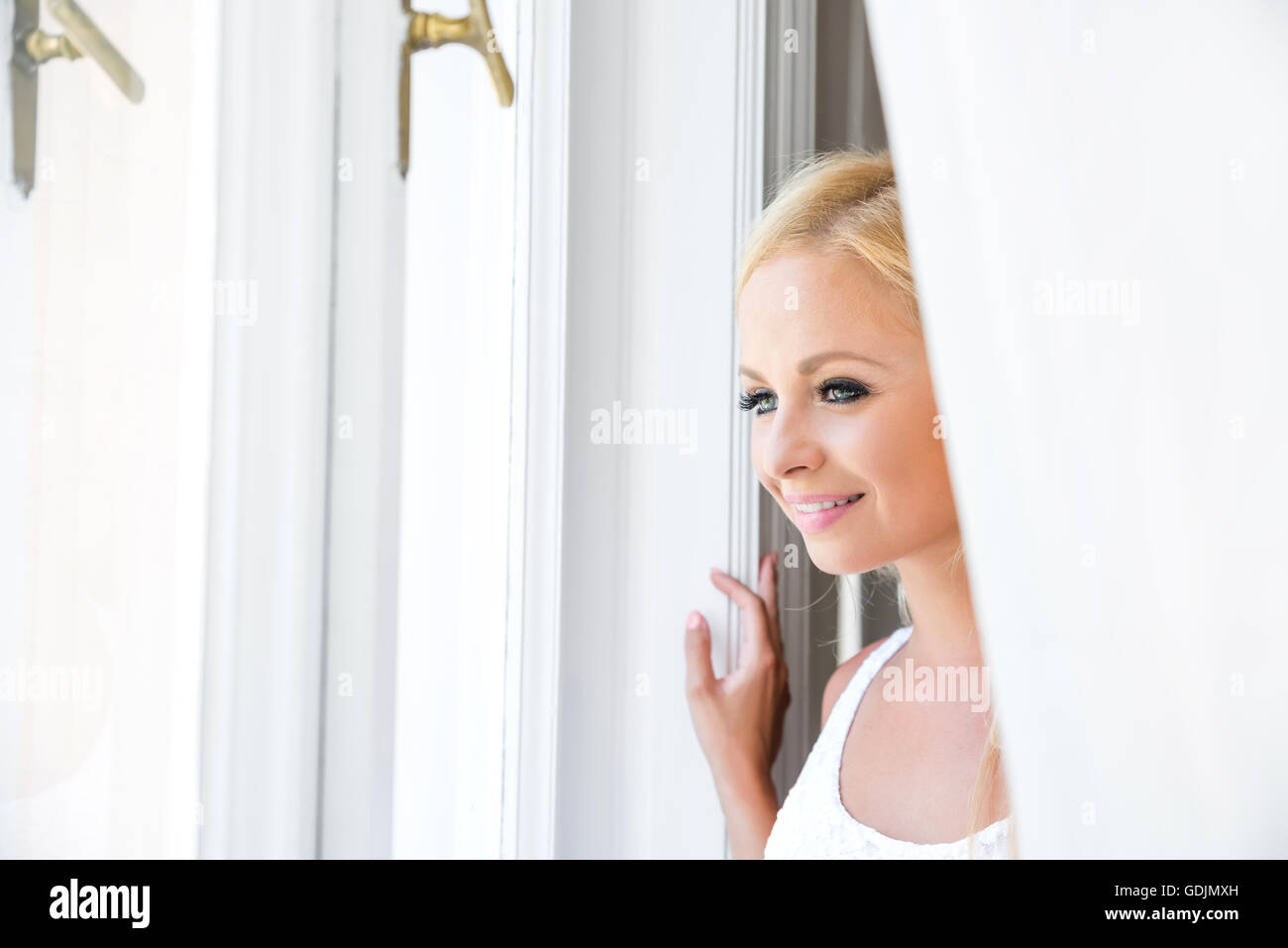 A beautiful young blond woman standing in the window Stock Photo - Alamy