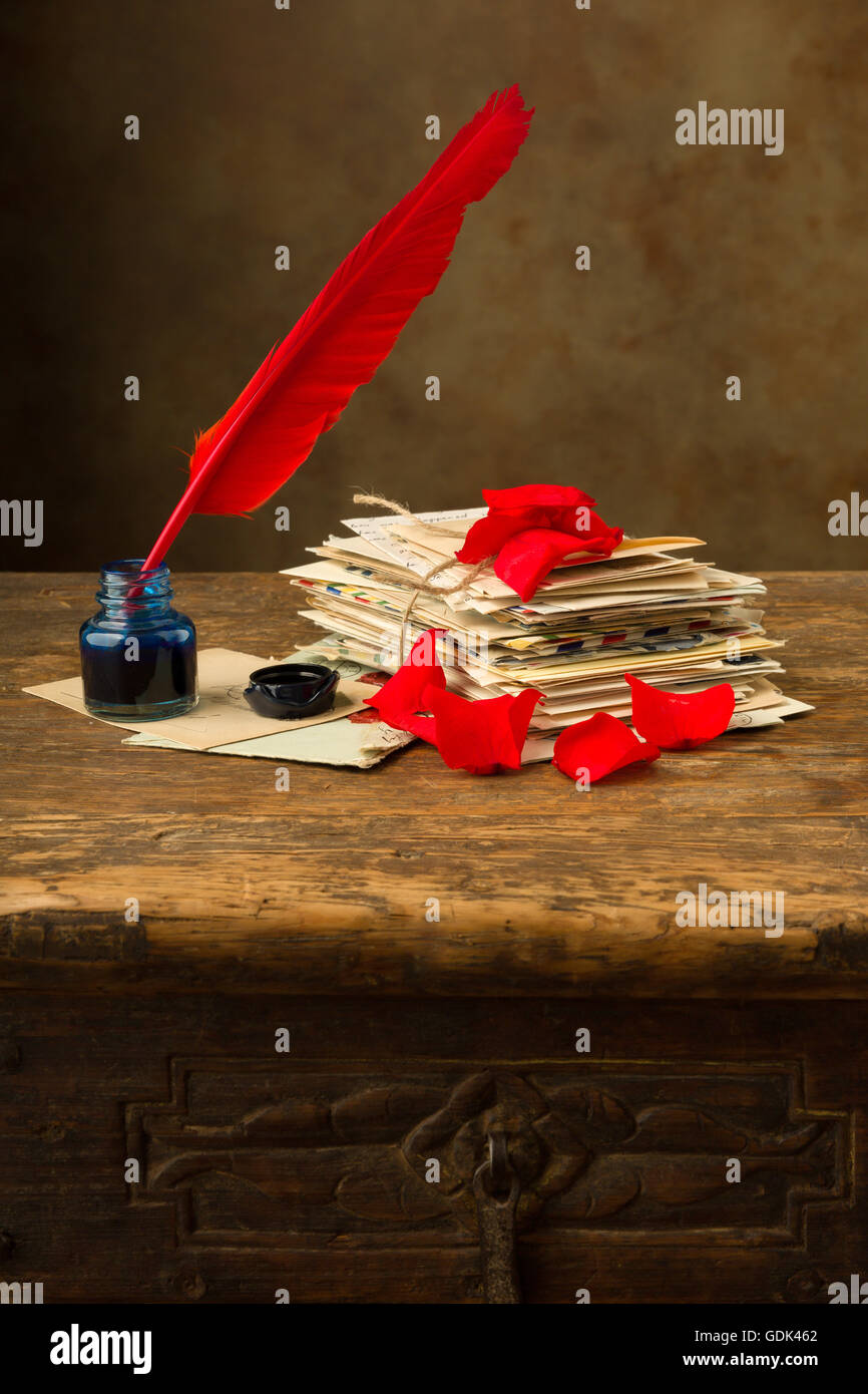 Red quill feather and ink well lying on an old table with nostalgic ...