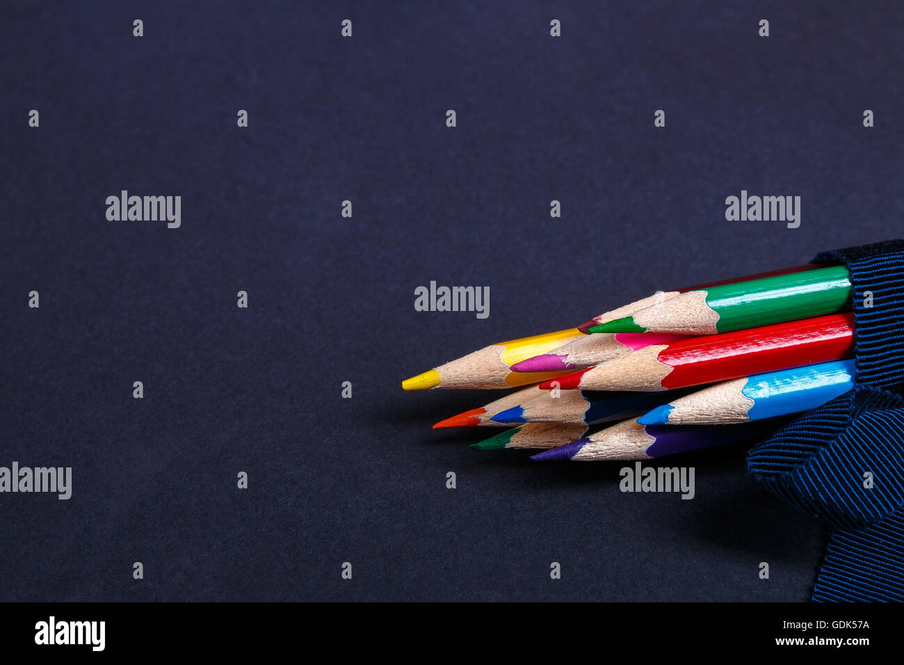 Set of colored pencils wrapped in a blue ribbon on black background ...
