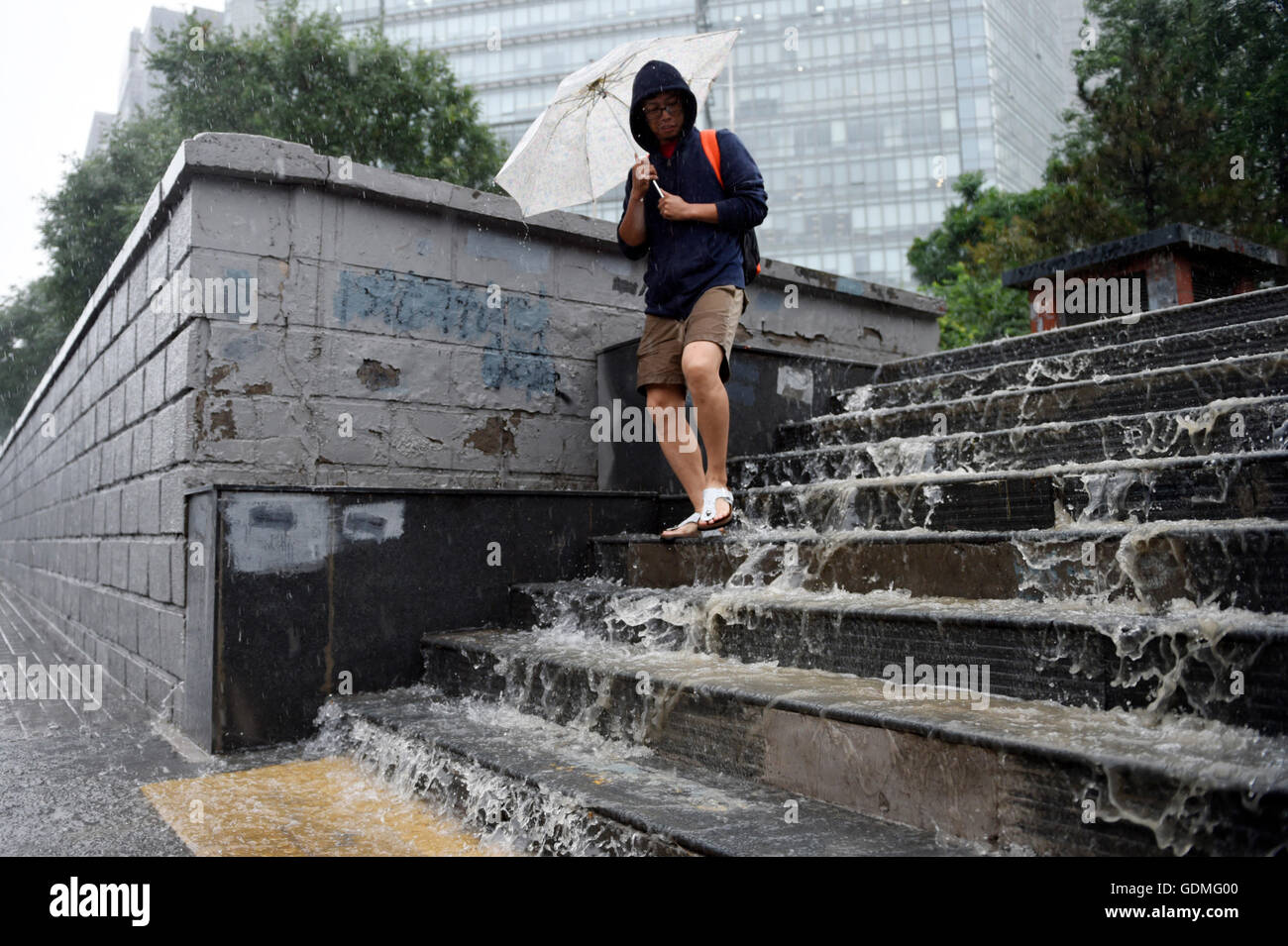 Beijing, China. 20th July, 2016. A resident walks in rain in Beijing ...