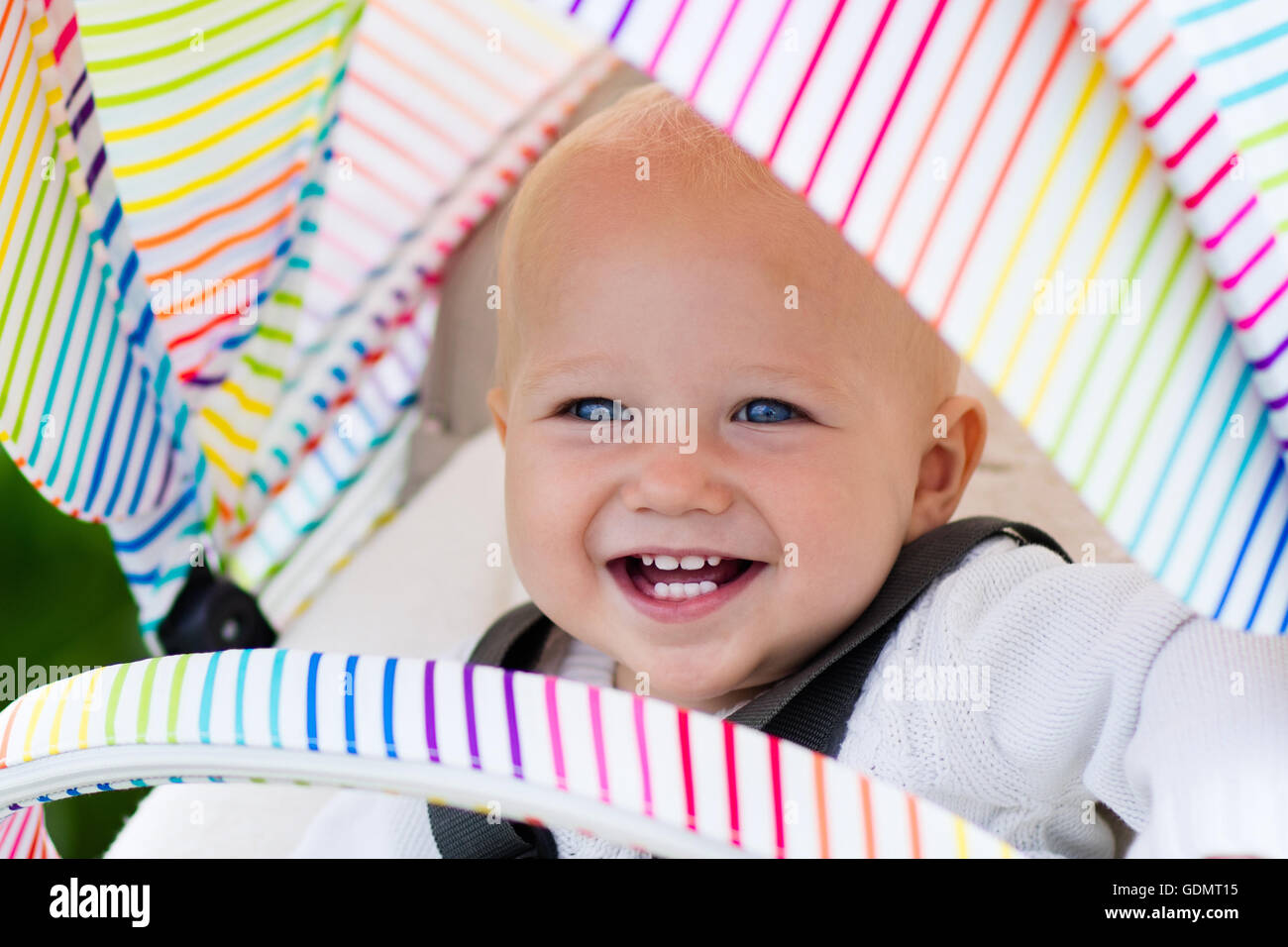 Baby boy in white sweater sitting in white stroller on a walk in park ...