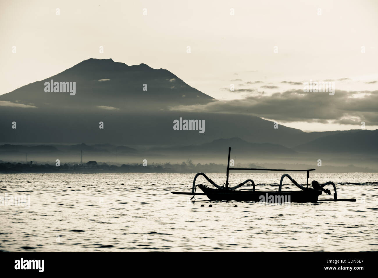 An outrigger canoe achored with a volcano peak above the clouds in the ...