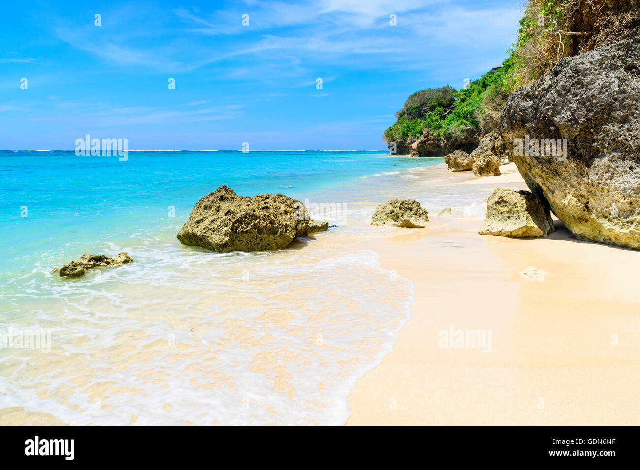 Tropical beach in Bali with rocks and small waves washing over the sand ...