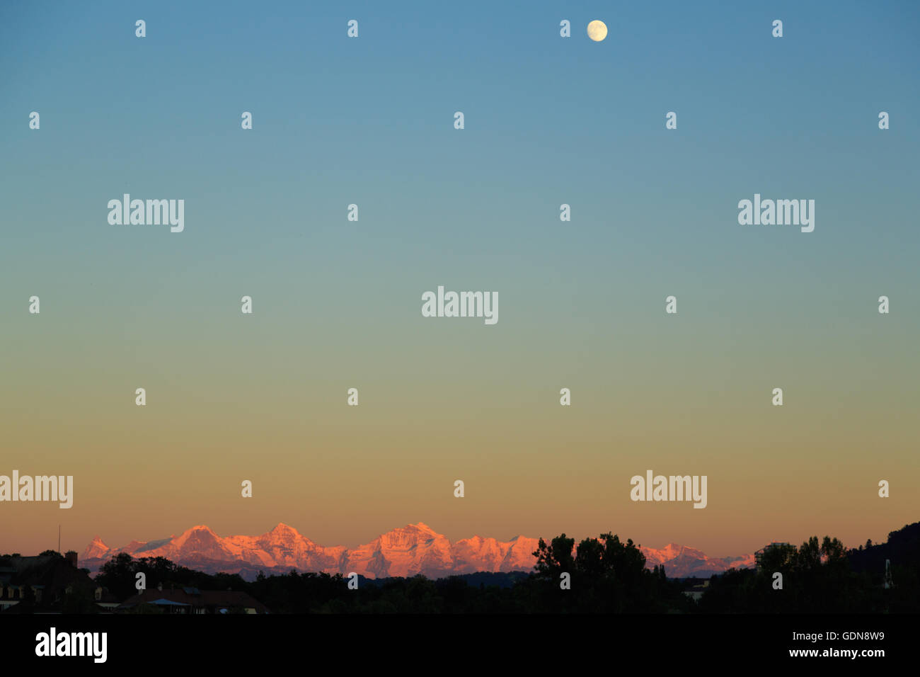 A photograph of the Swiss Alps with the moon high above them, as seen ...