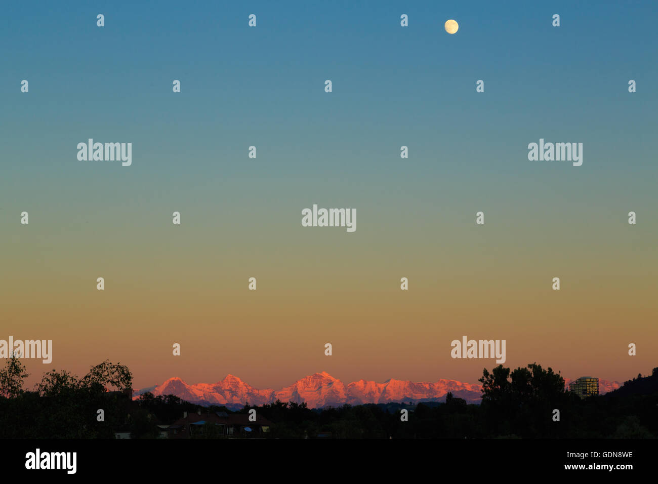 A photograph of the Swiss Alps with the moon high above them, as seen ...