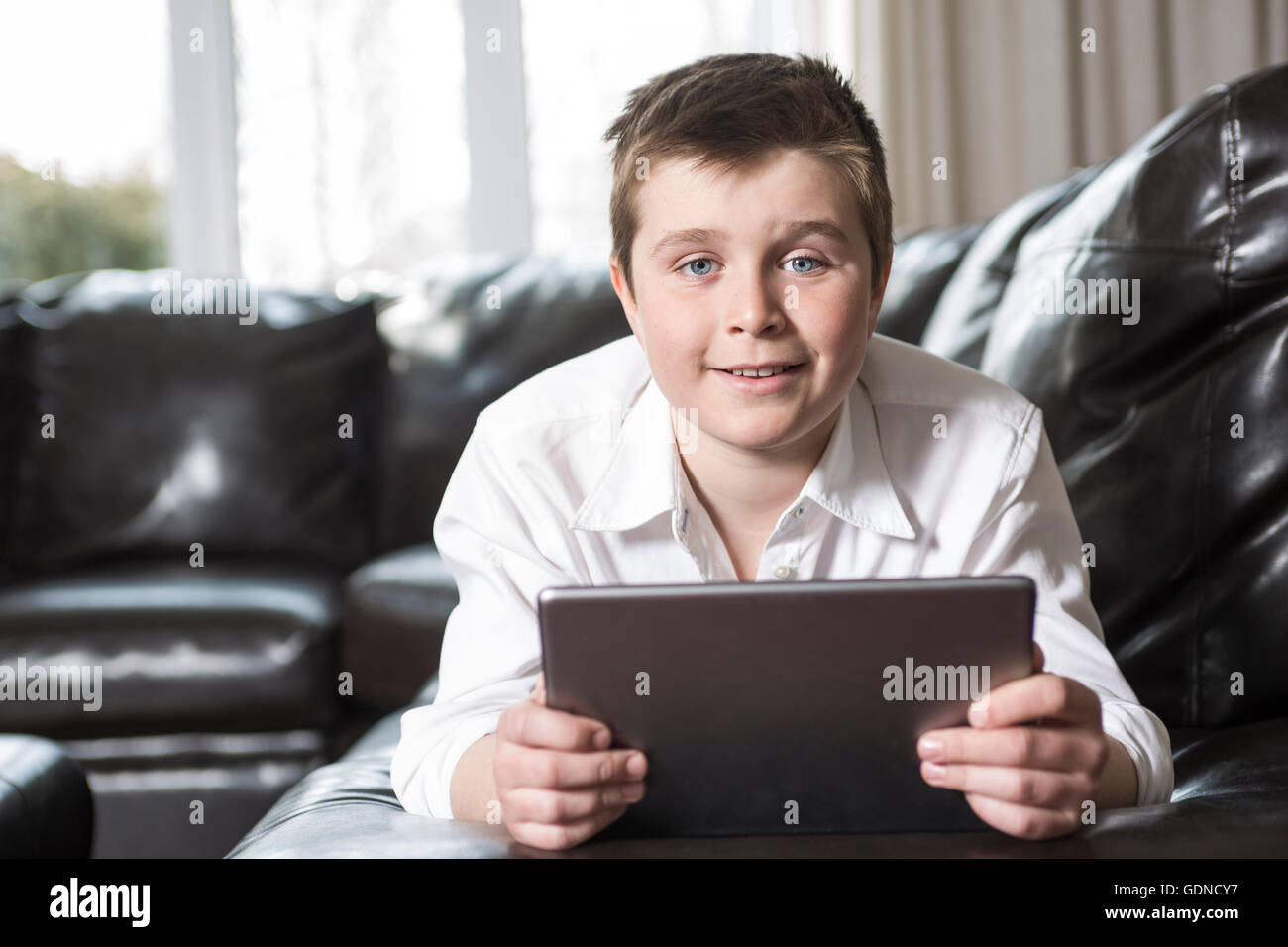 young boy child resting on his hands laying down a sofa using tablet ...