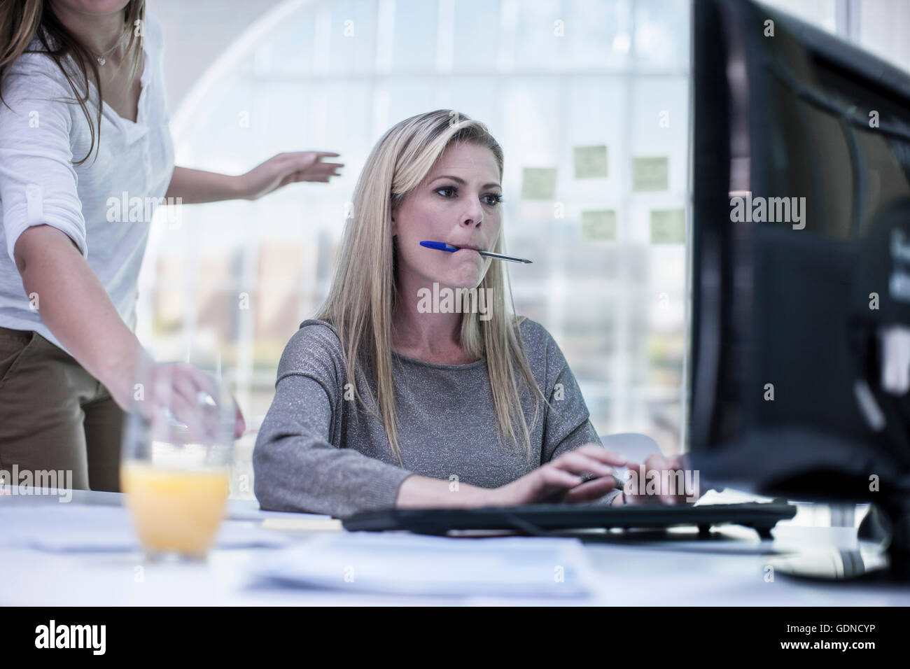 Female designer with pen in her mouth, typing on desktop computer in ...