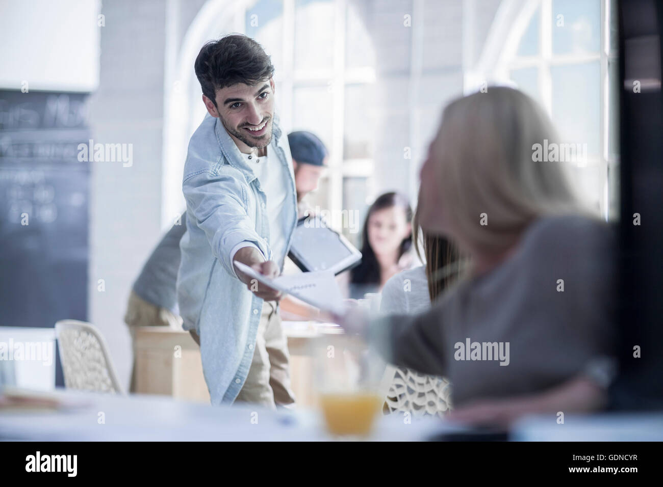 Male designer handing over paperwork in design studio Stock Photo - Alamy