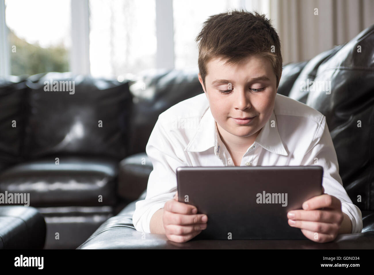 young boy child resting on his hands laying down a sofa using tablet ...
