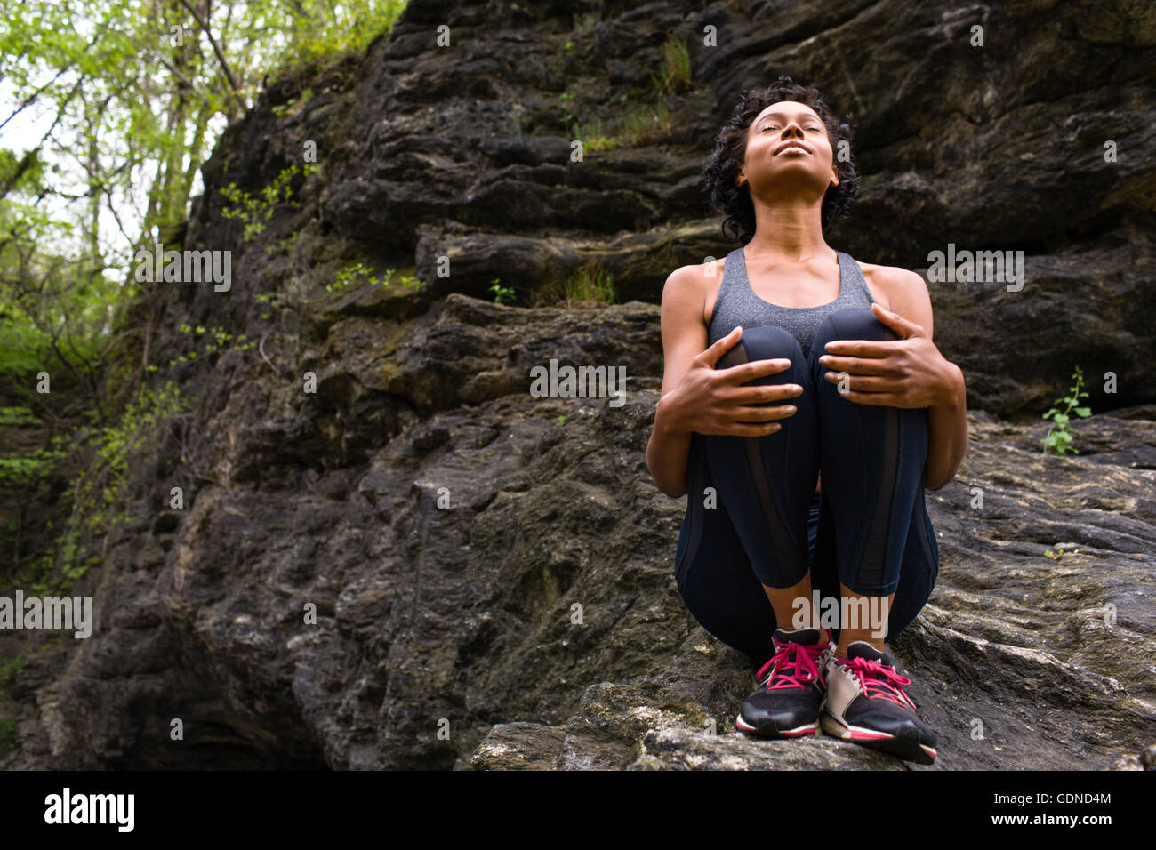 Woman sitting hugging knees on rock meditating Stock Photo - Alamy