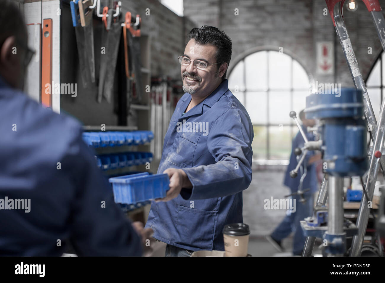 Worker handing over tray in workshop Stock Photo - Alamy