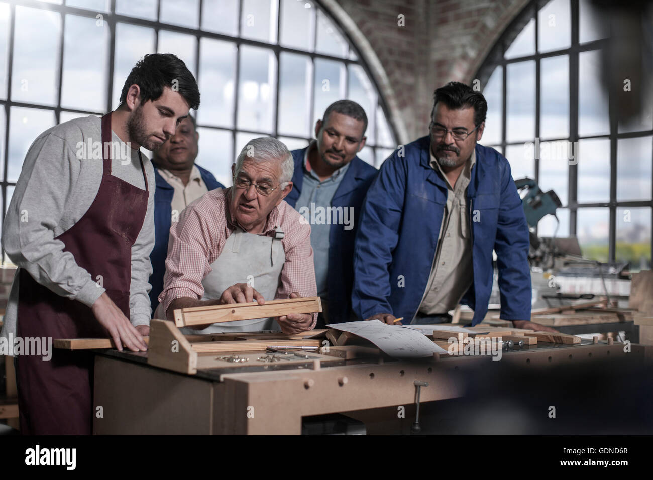 Senior carpenter demonstrating to trainee and team in workshop Stock ...