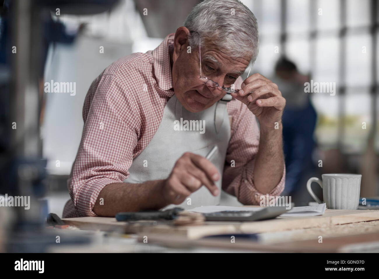 Senior carpenter using calculator in wood workshop Stock Photo - Alamy