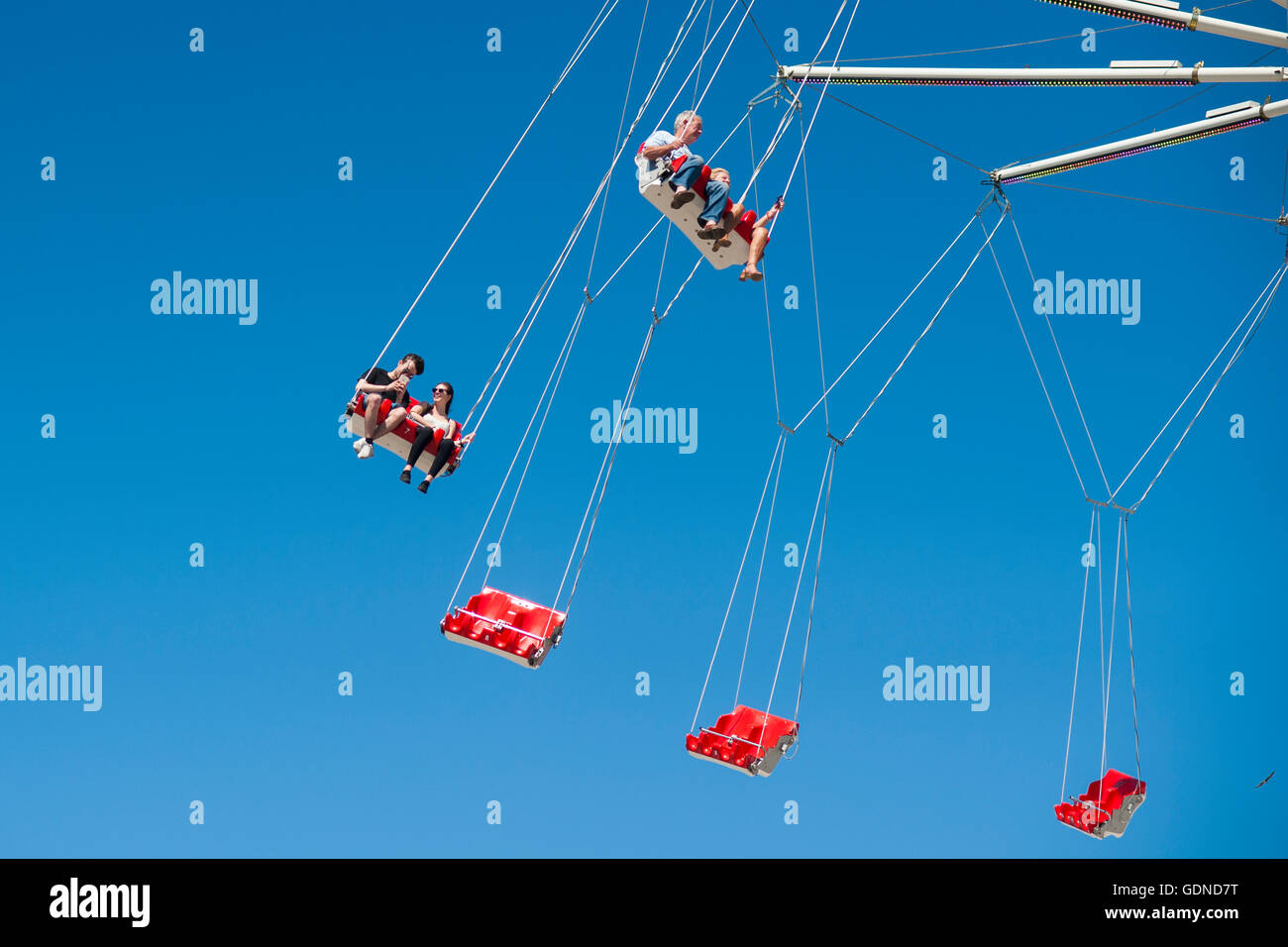 People on fairground ride swings high up in the air with a blue sky ...