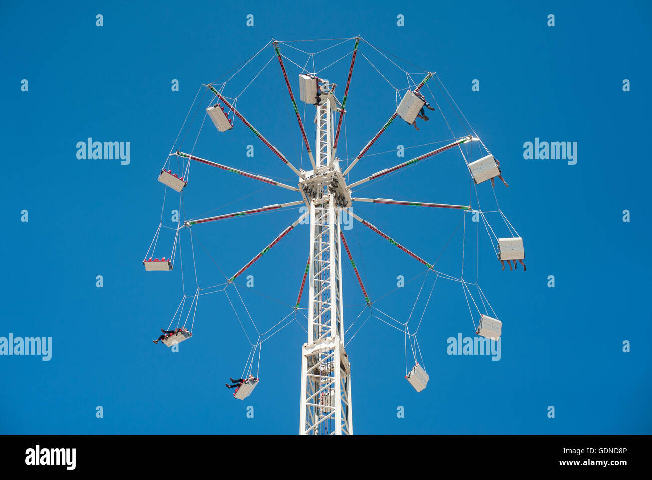 People on fairground ride swings high up in the air against a bright ...