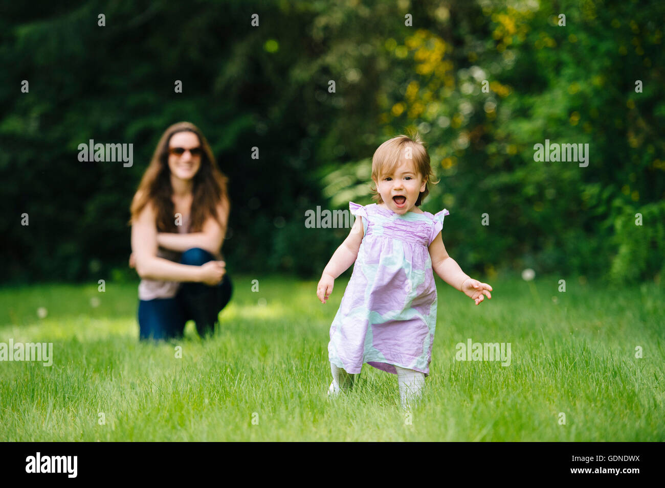 Female toddler running away from watching mother in park Stock Photo ...