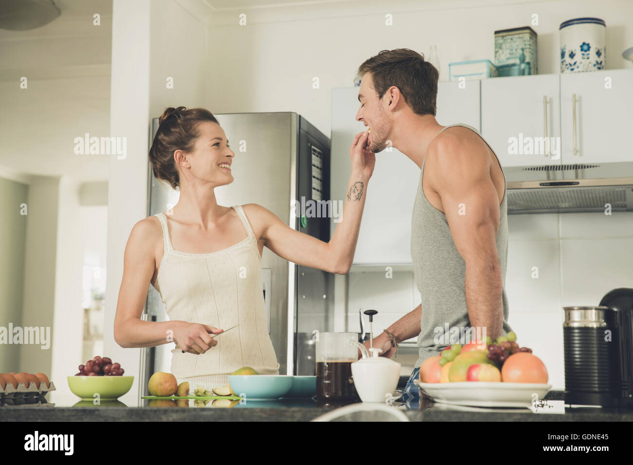 Young woman feeding fruit to boyfriend at kitchen counter Stock Photo ...