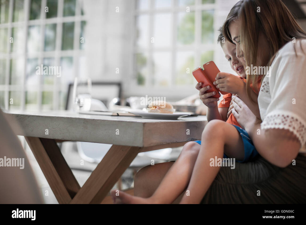 Mother and son using smartphone at dining table Stock Photo - Alamy