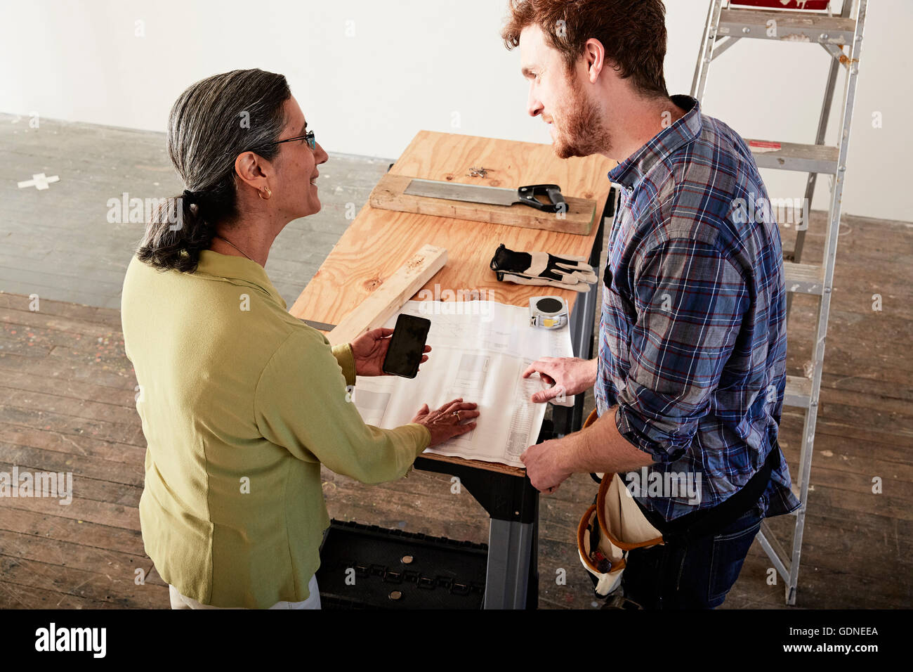 Carpenter looking at blueprint with client Stock Photo - Alamy