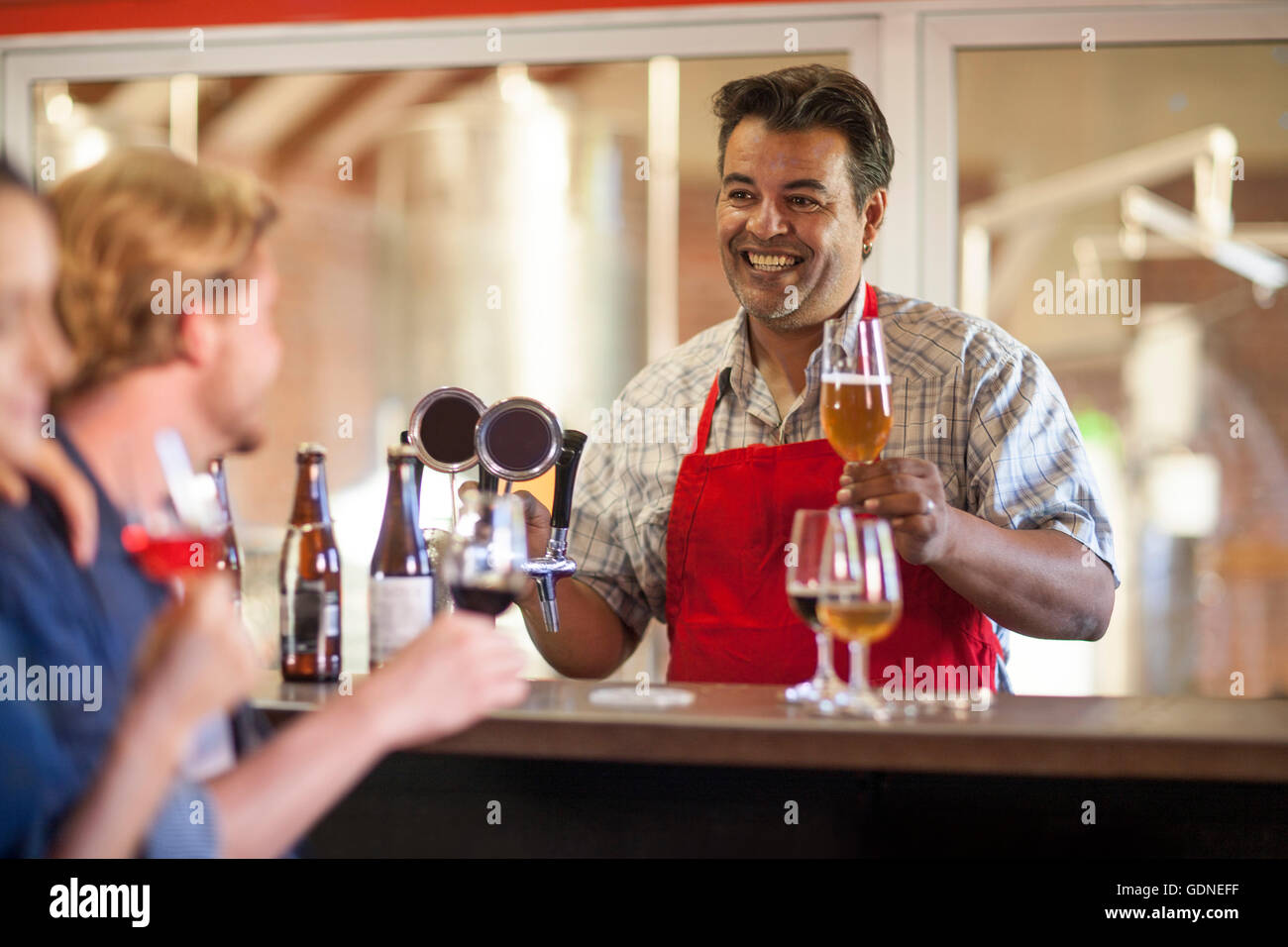 Bartender in public house serving customers beer smiling Stock Photo ...