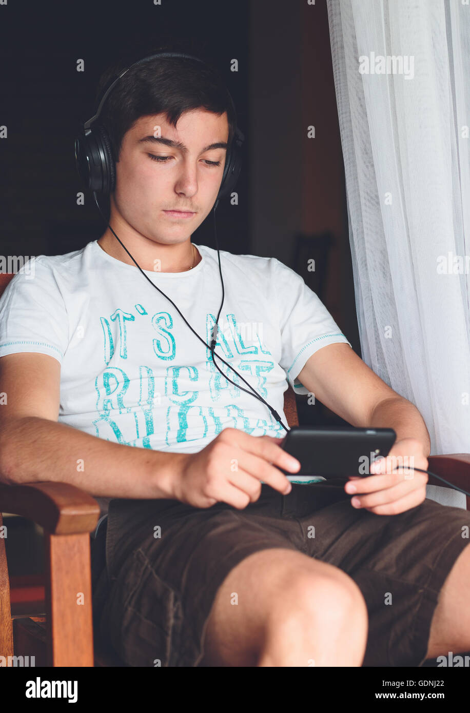 Relaxed young boy sitting at the patio door and listening to music from ...