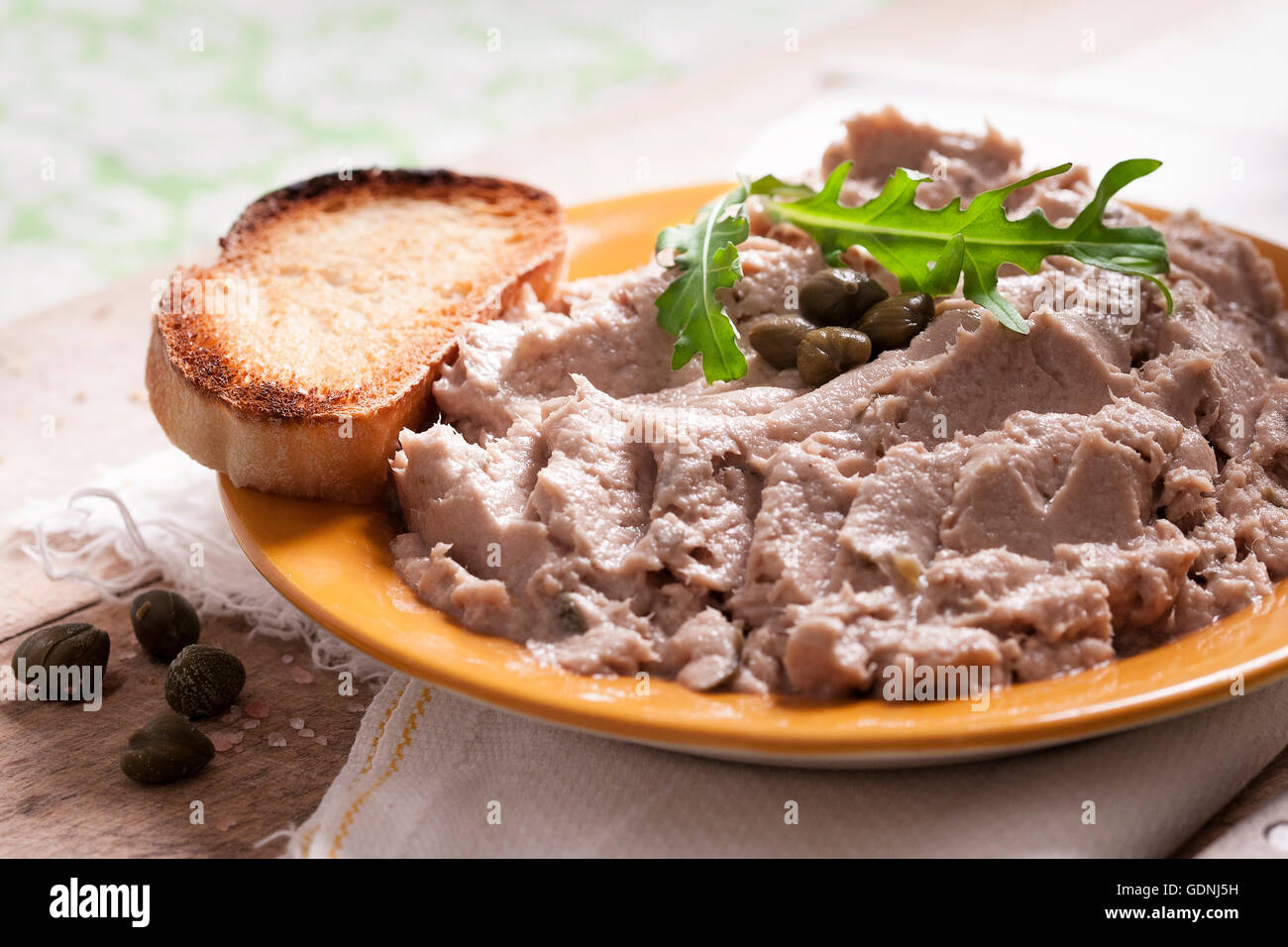 Fish pate spread with toast, capers and rucola on a wood board close up ...