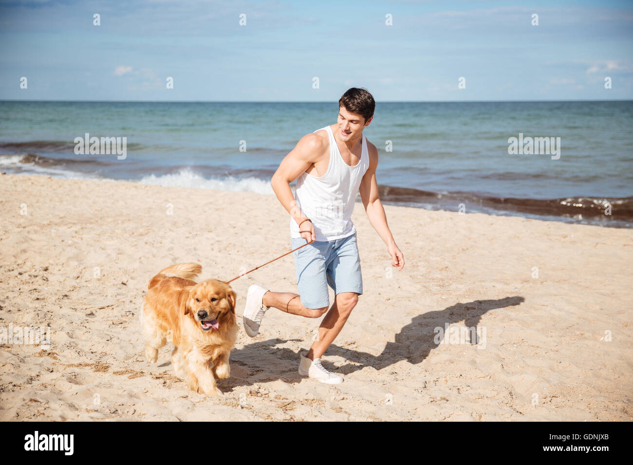 Smiling handsome young man jogging with his dog on the beach Stock ...