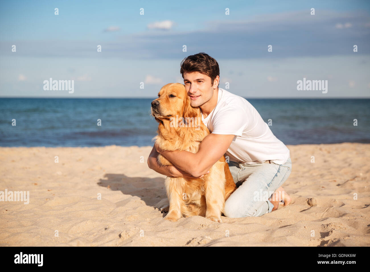 Handsome young man sitting and hugging his dog on the beach Stock Photo ...