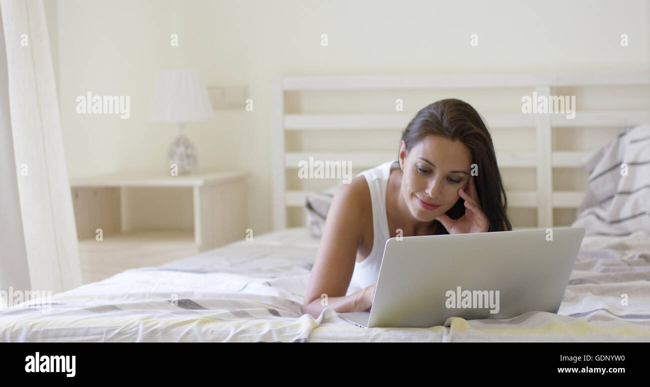 Young woman laying down in bed using laptop Stock Photo - Alamy