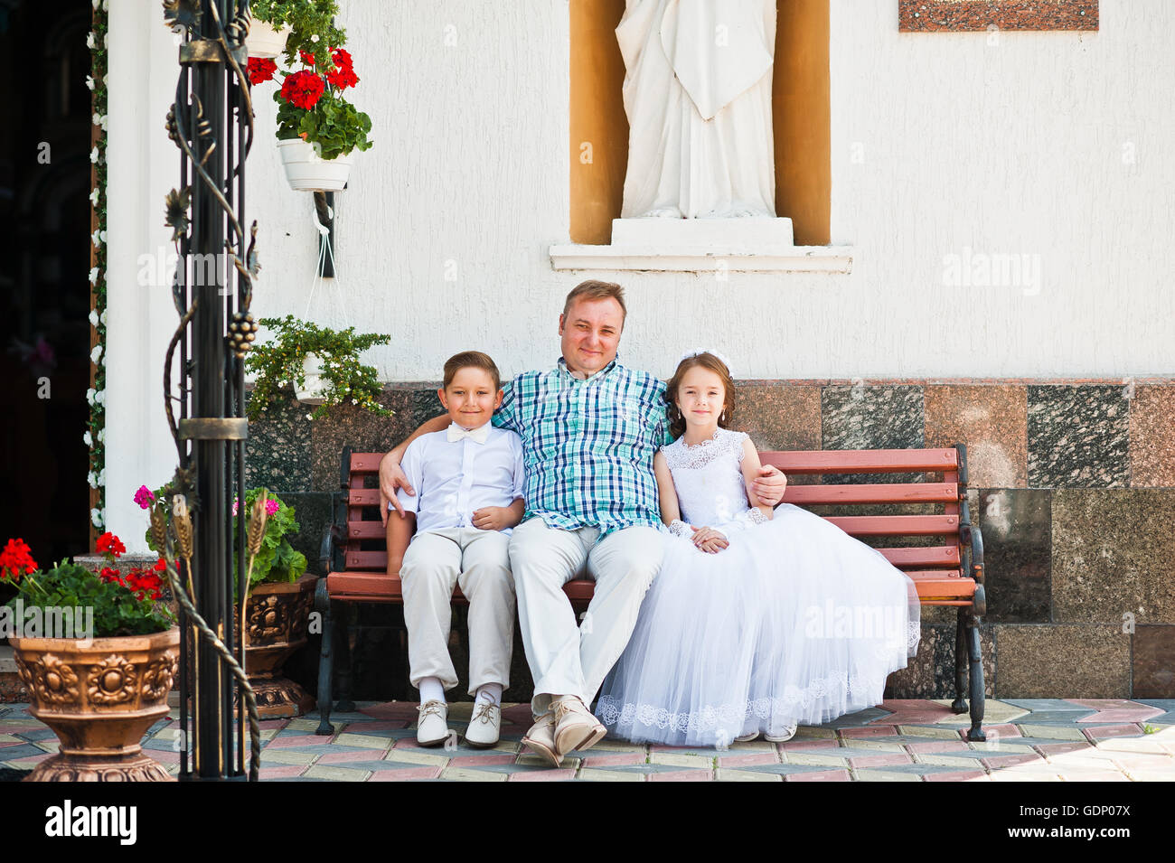 Happy family at first holy communion sitting on bench background church ...