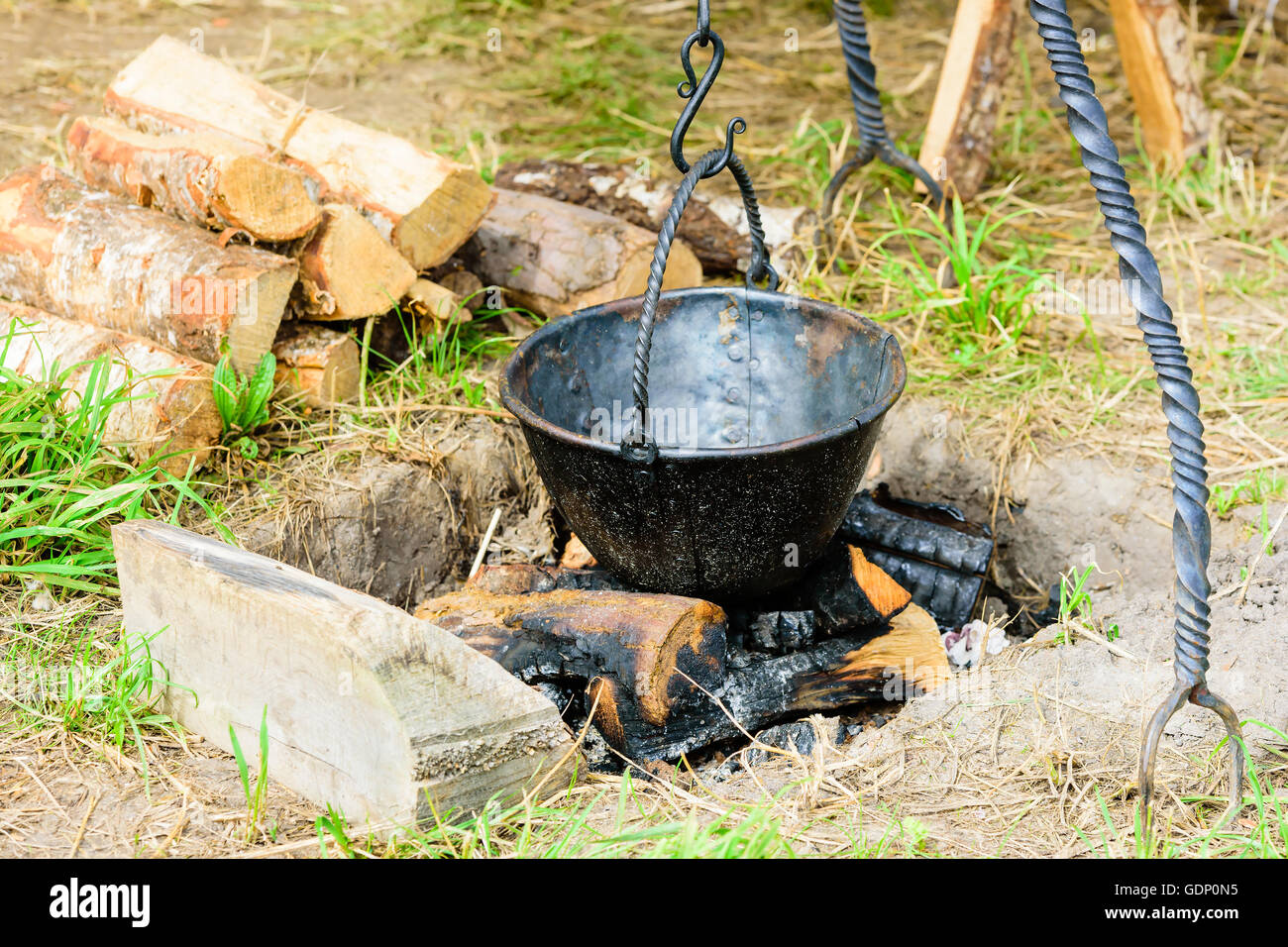 Empty outdoor cooking pot hanging over burnt wood and ashes. Pot is ...