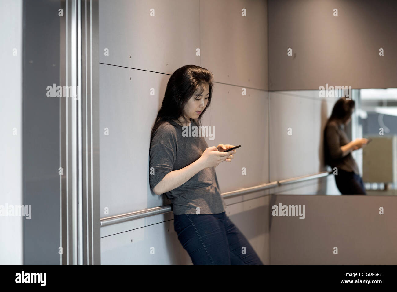 Woman leaning against wall, using smartphone Stock Photo - Alamy