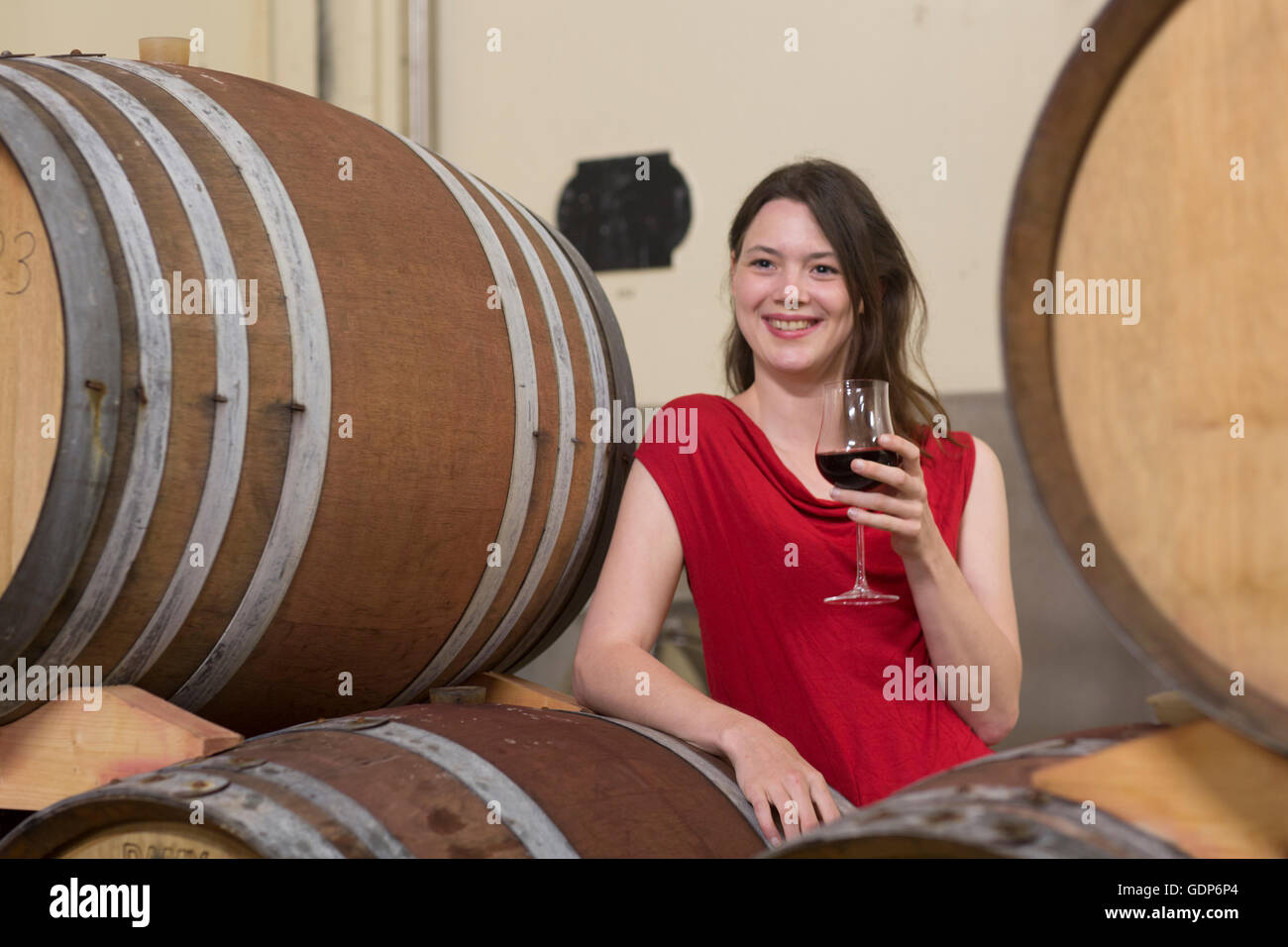 Portrait of young woman in wine cellar, leaning against wine barrel ...