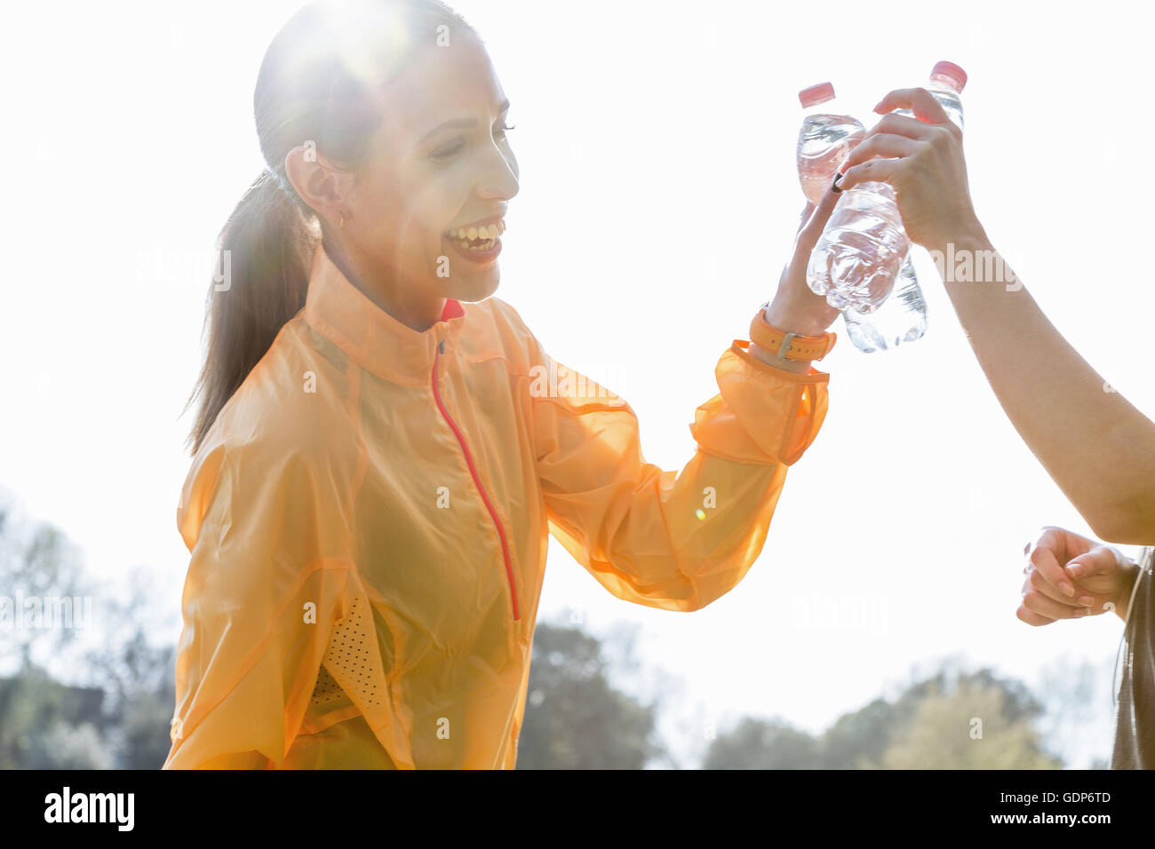 Two female friends outdoors, holding water bottles, making toast with ...